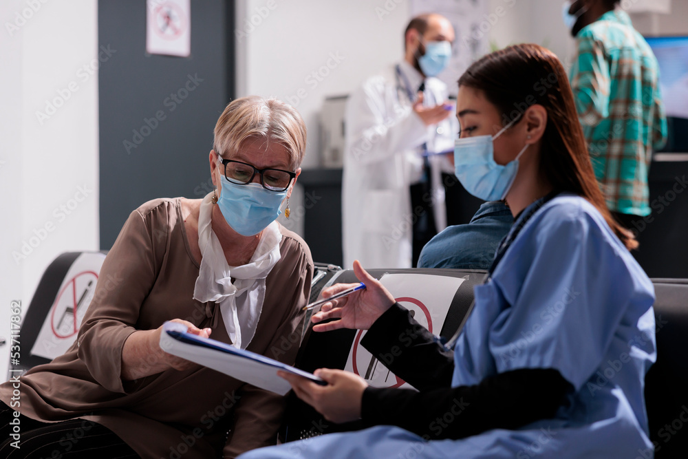 Asian nurse filling out file of mature adult patient at medical clinic ...