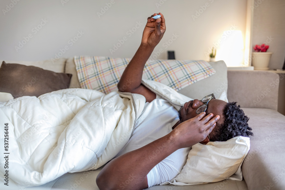Young sick african guy with fever, checking body temperature with ...