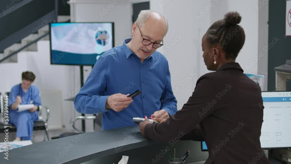 Senior man paying with credit card at hospital reception desk, making ...