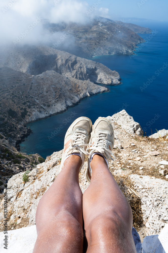 Girl legs on top of a cliff in Folegandros Island. Cyclades of Greece ...