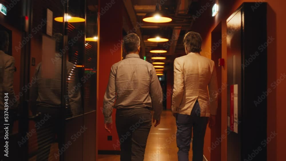 Male colleagues in suits walking down in hallway together, talking ...