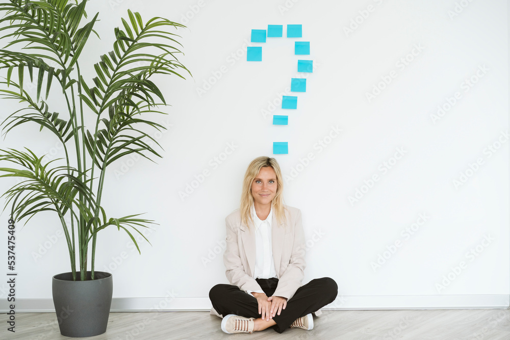 Businesswoman sitting on the floor in office with question mark above ...