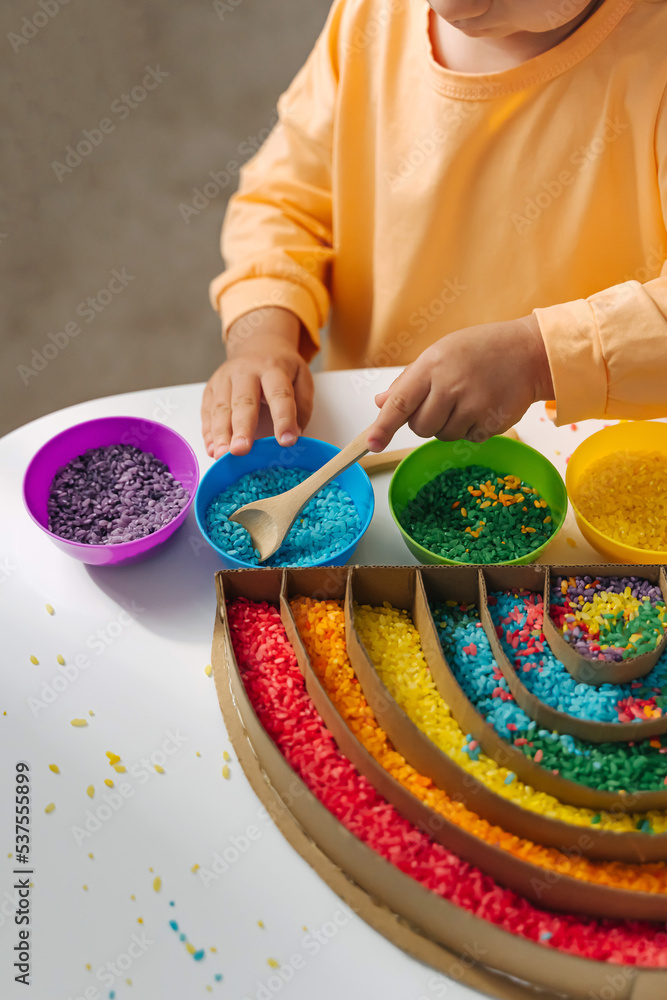 A little girl playing colored rice and make rainbow. Child filled the ...