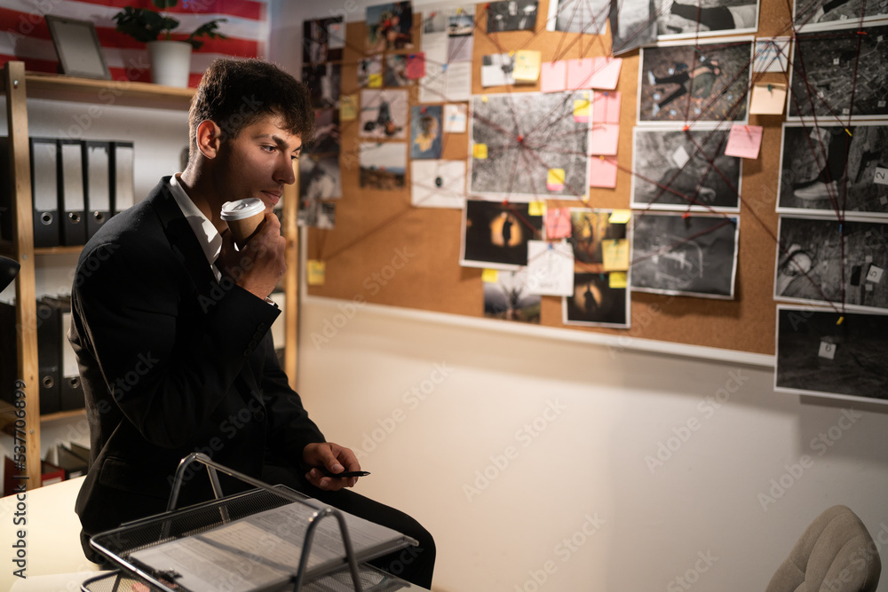 Detective working in his office interior with evidence board on wall ...