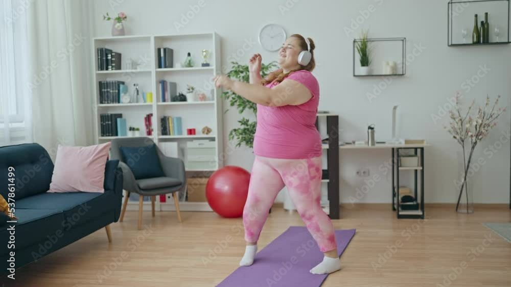 Excited plus size young woman dancing, listening music in headphones ...
