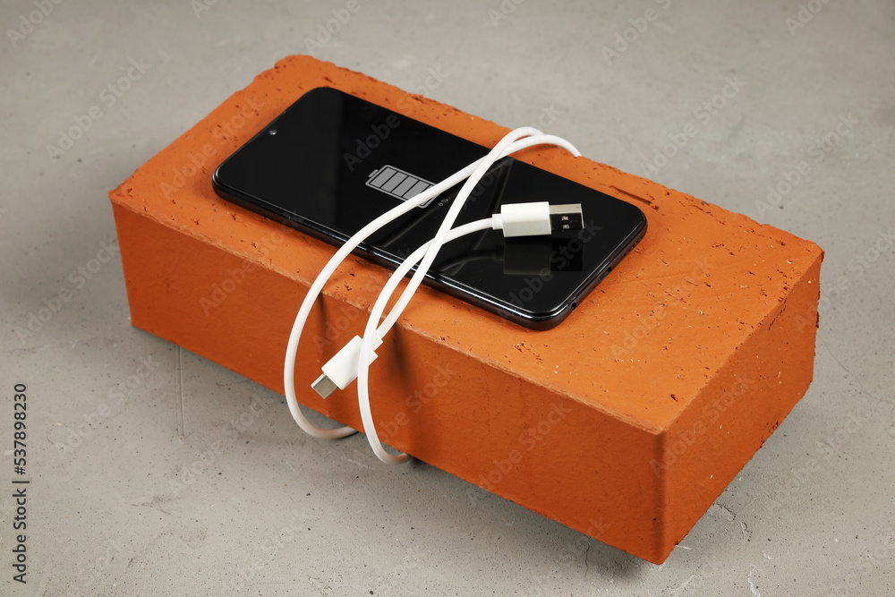 Smartphone with low charge of battery lies on red brick, around ...