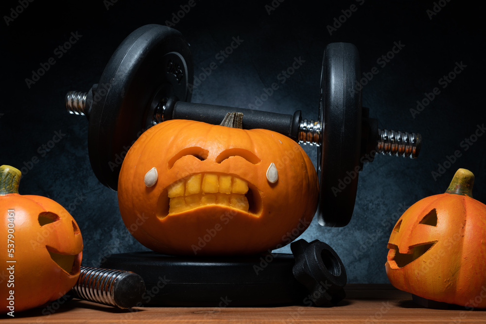 Carved Halloween pumpkin lifting a heavy barbell dumbbell ...
