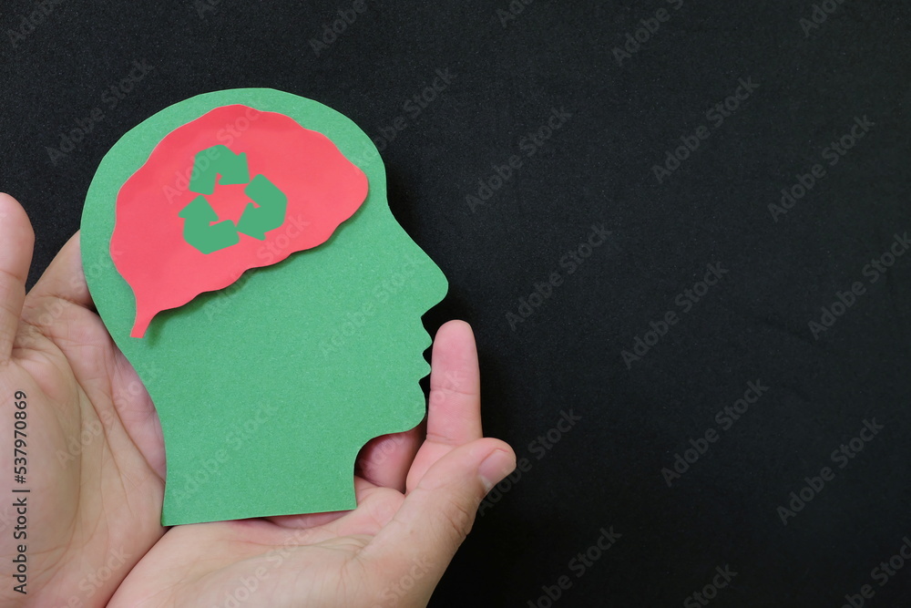 Human hands holding human head cutout with recycling icon in brain. Nurture environment friendly ...