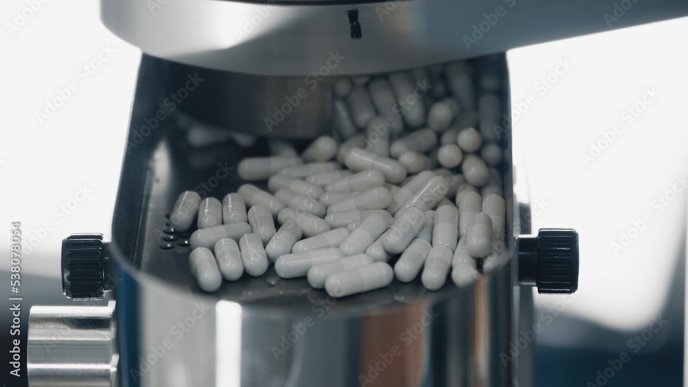 White capsules fall from a metal conveyor. Automatic line in modern ...