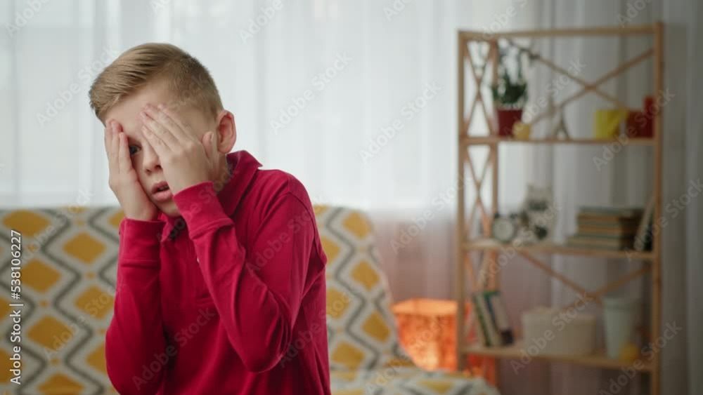 Scared boy covering eyes with hands. Horrified boy in red polo shirt ...