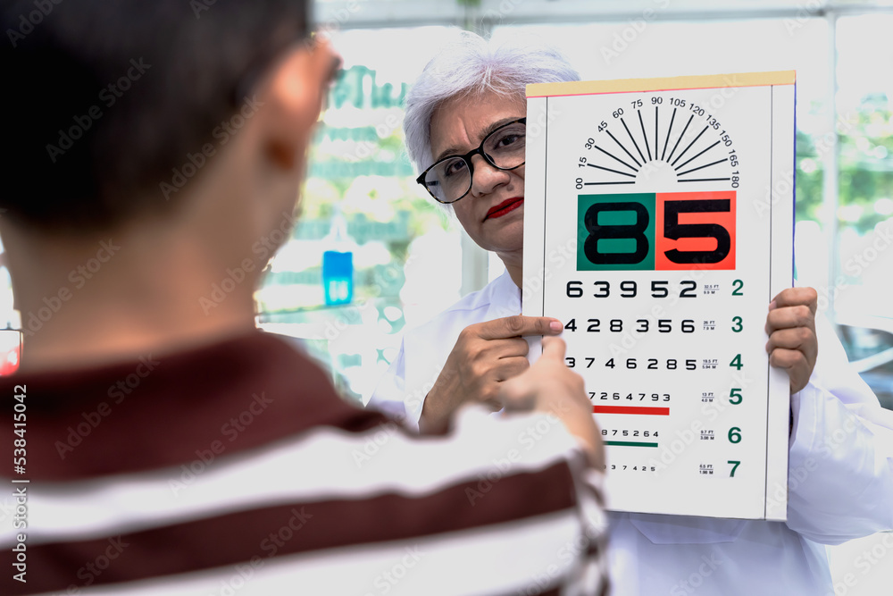 Old Indian optician woman showing snellen eye testing chart to boy ...