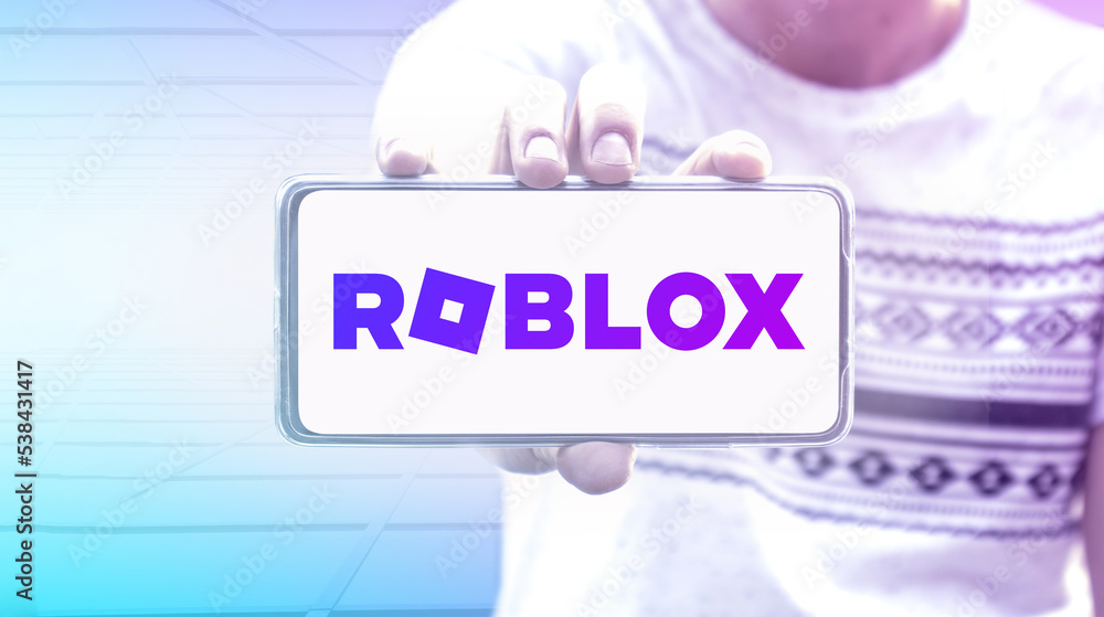 Roblox logo word on smartphone hold by a hand inside the metaverse ...