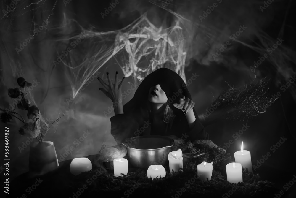 A young witch in hood does black magic ritual using the Witch's book ...