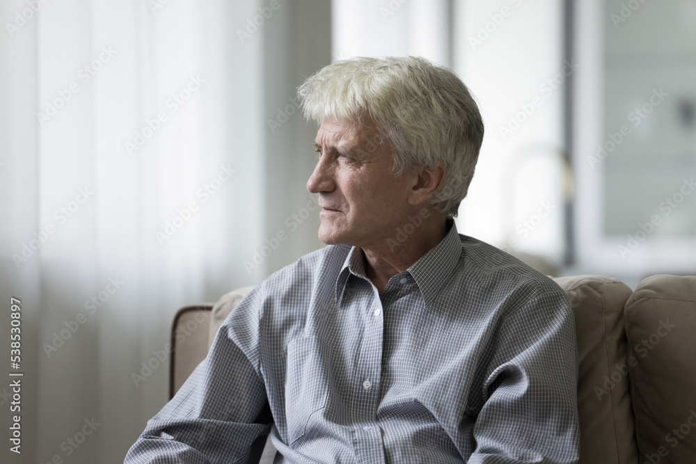 Gloomy elderly man sitting on sofa staring into distance, feels ...