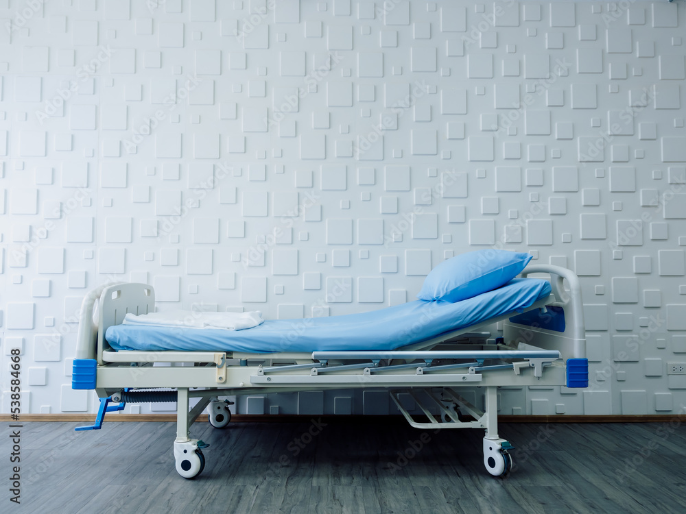 An empty adjustable patient bed with blue bedsheet and pillow on white ...