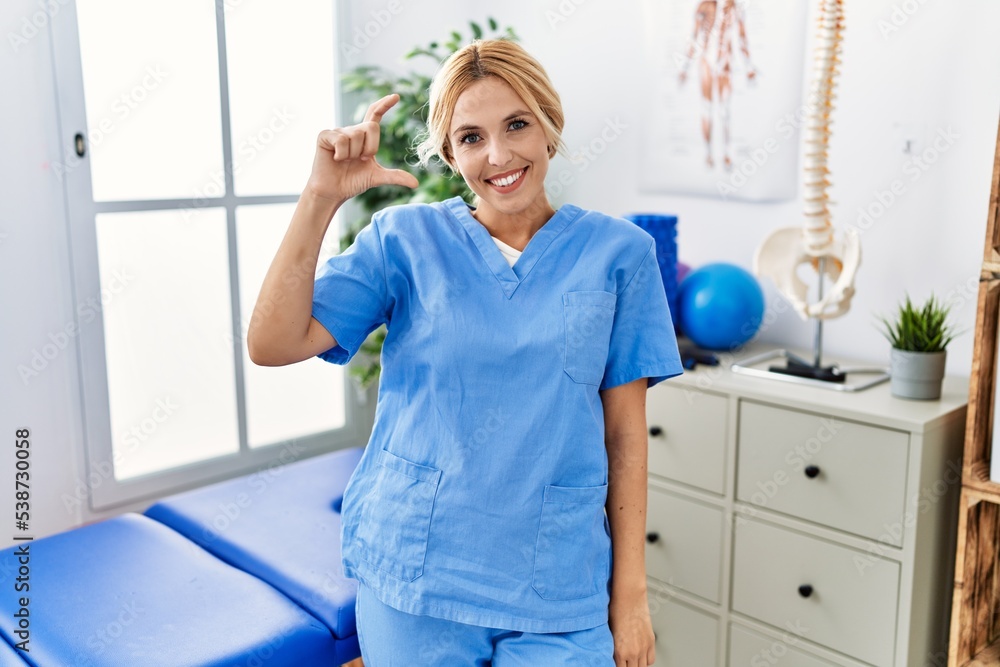 Beautiful blonde physiotherapist woman working at pain recovery clinic ...