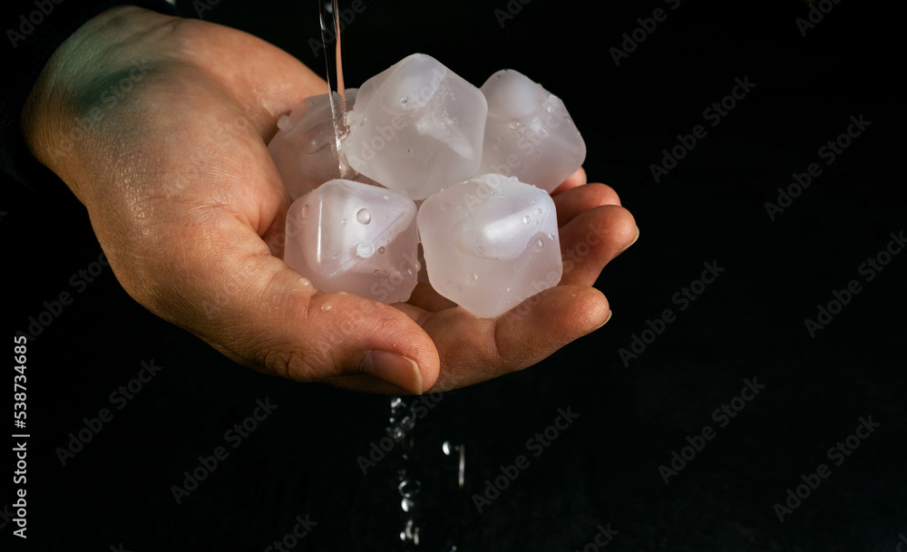 White woman's hand holding ice blocks on a dark background. Mention of ...
