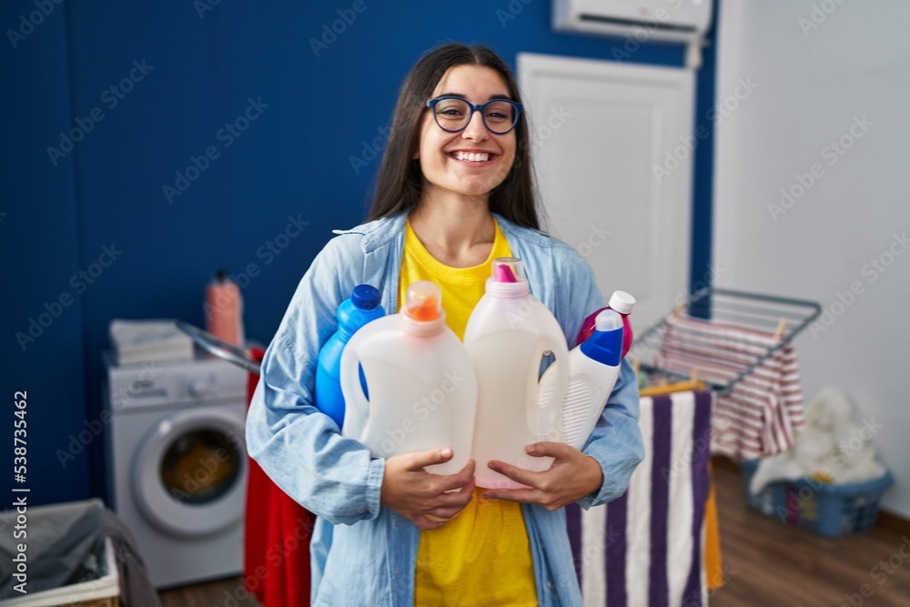 Young hispanic woman holding detergent bottles celebrating crazy and amazed for success with ...