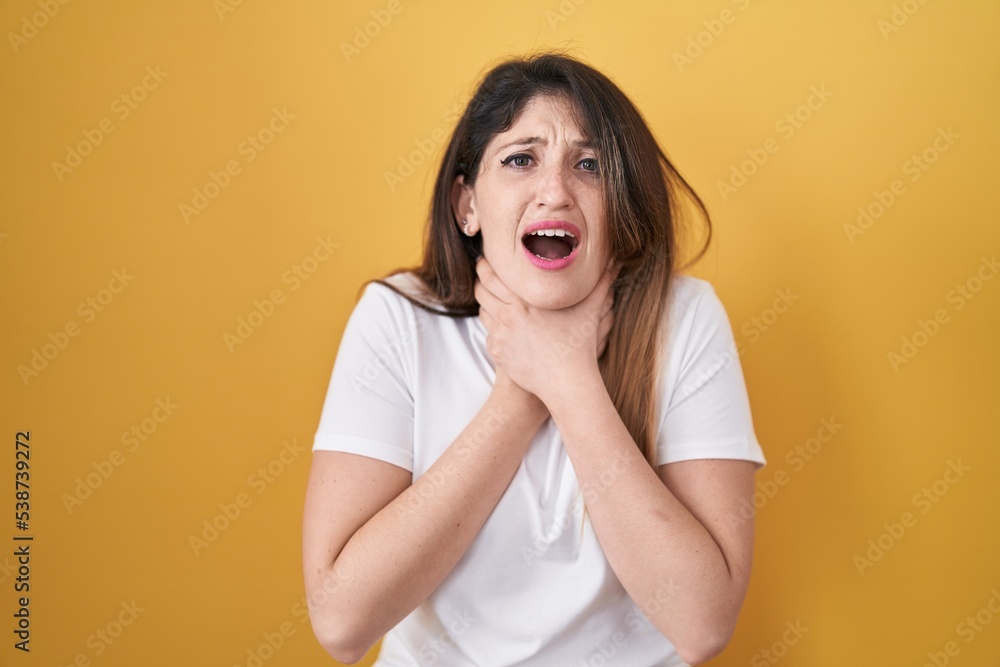 Young brunette woman standing over yellow background shouting and ...