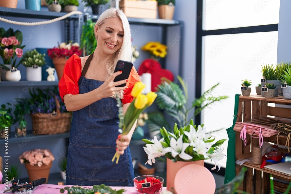 Young blonde woman florist make photo to flowers at florist store Stock ...