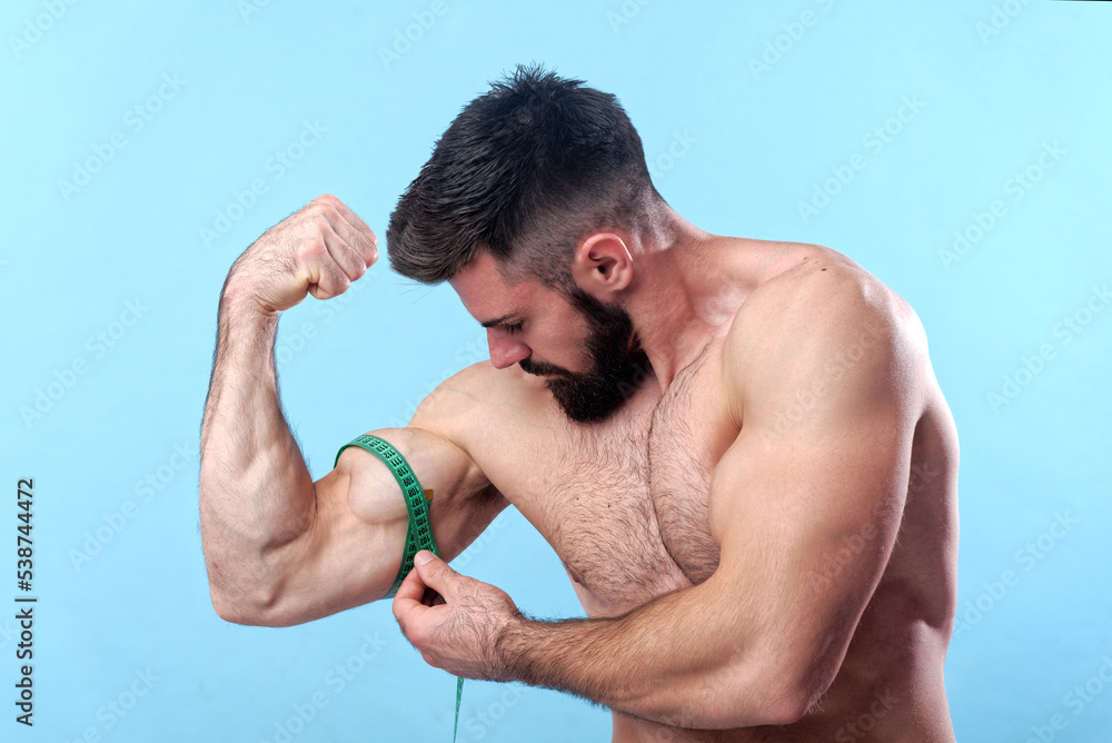 Young shirtless man, a bodybuilder, measuring his biceps size using a ...