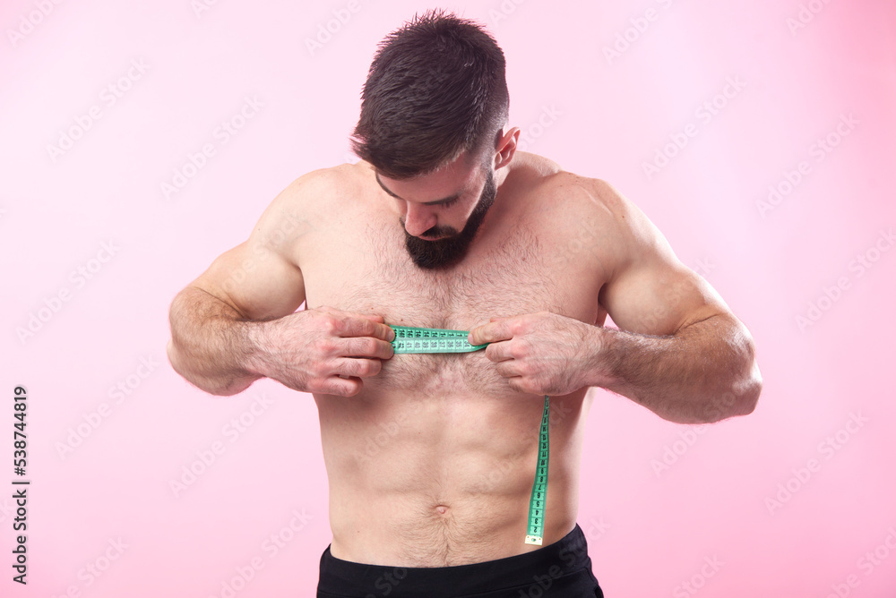 Strong shirtless bodybuilder measuring his chest width with a measuring ...