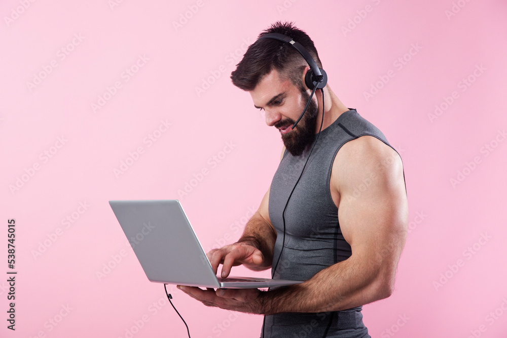 Young bodybuilder, online fitness coach, using a laptop and a headset ...