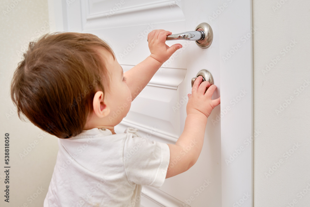 Toddler baby opens the lock, holding the door handle, child hand close ...