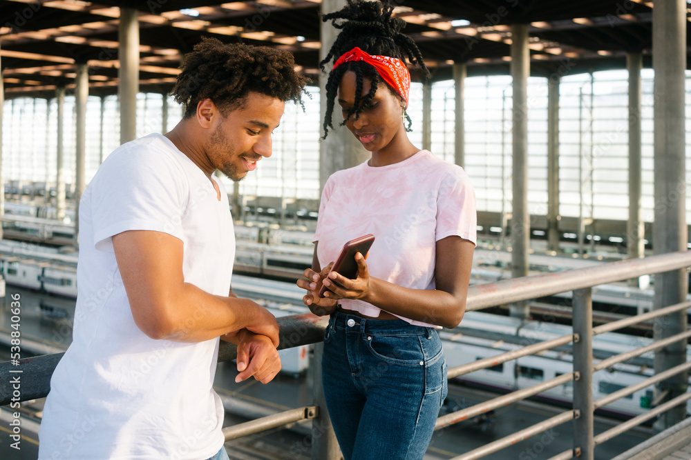 Young woman sharing mobile phone with friend at railroad station Stock ...