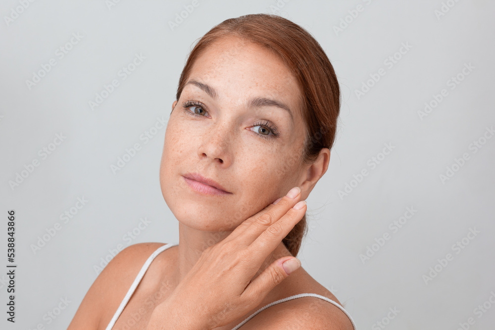Portrait of cropped caucasian middle aged woman face with freckles holding fingers on cheek with ...