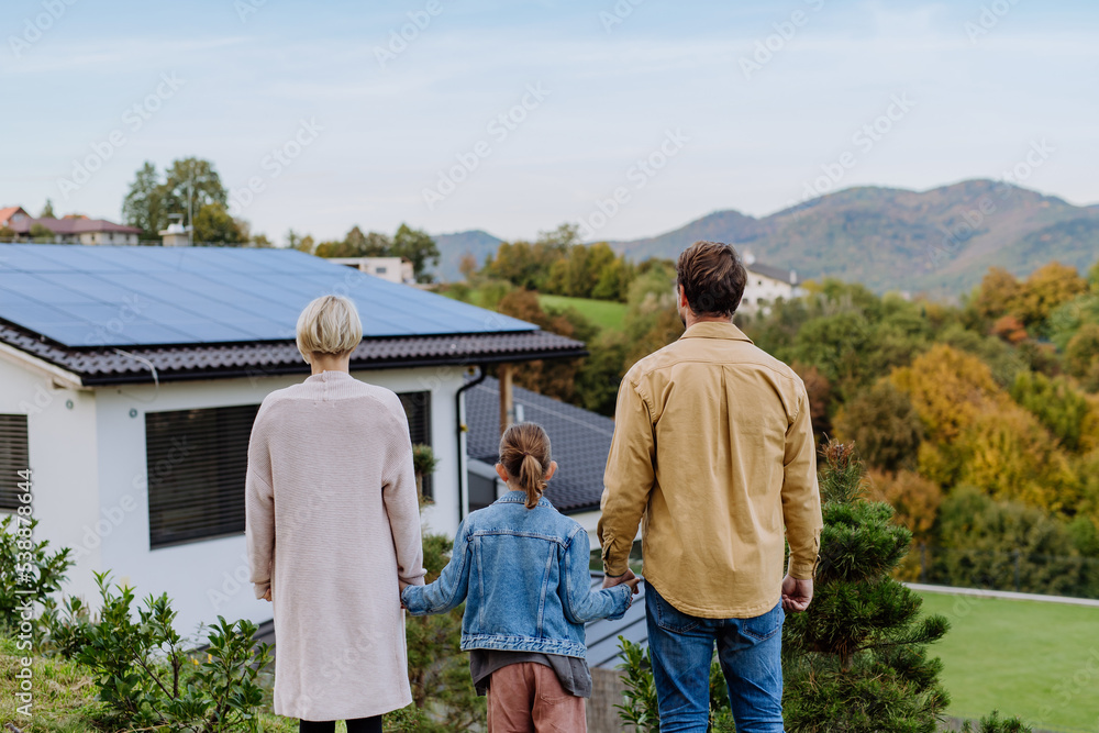 Rear view of family looking at their house with installed solar panels ...