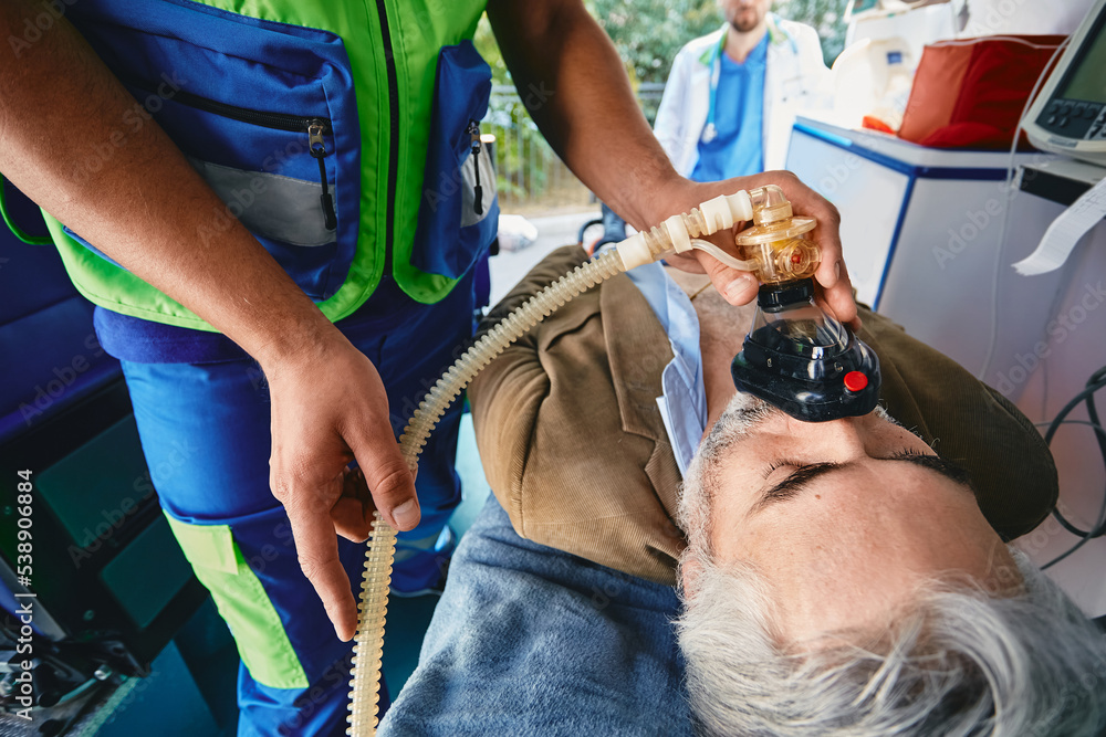Male paramedic providing medical help holding oxygen mask over patient ...