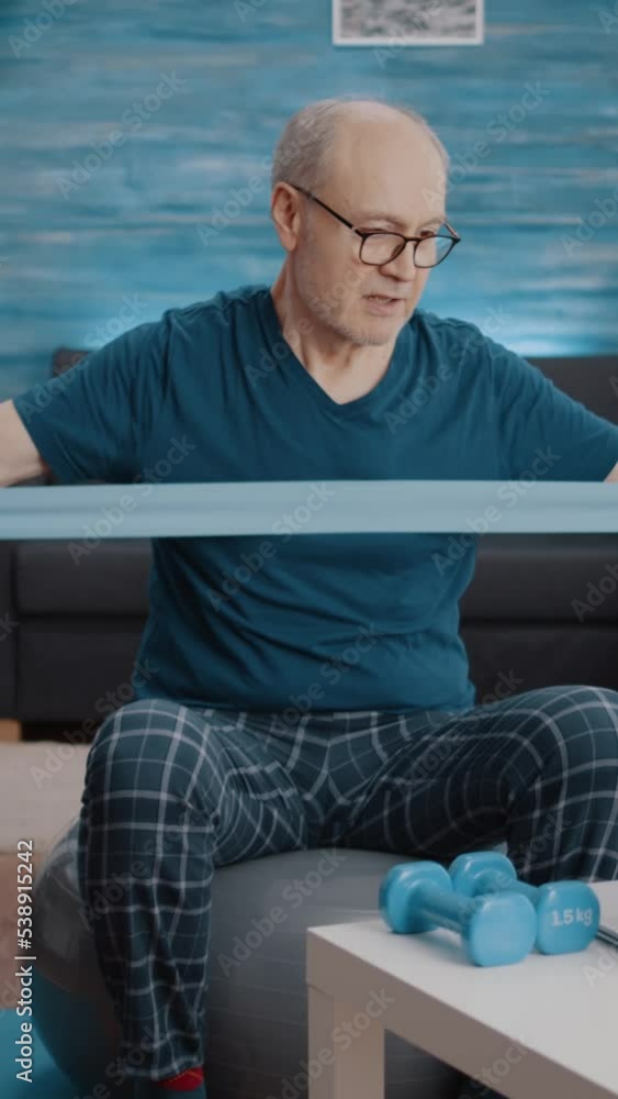Vertical video: Aged man pulling resistance band to stretch arms ...
