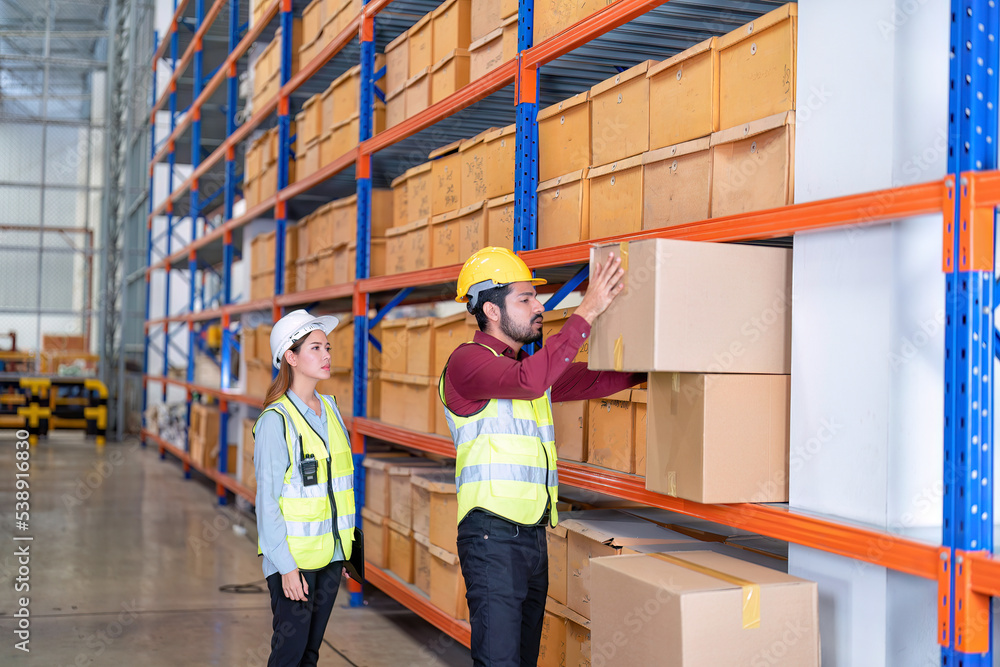 Warehouse worker hold the carton box walk along the steel racking shelf ...