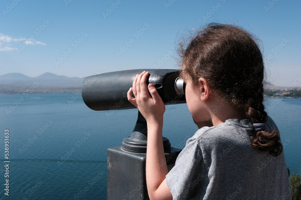 10-year-old boy looks through coin operated binocular (binoscope) at ...