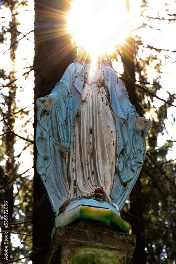 The statue of the Virgin Mary in the forest is shining of sun´s rays ...