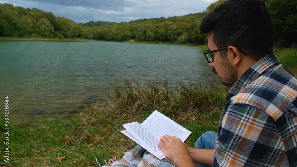 Vidéo Stock Man with glasses reading book by the lake side view ...