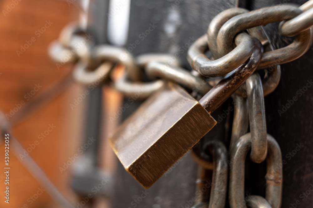 Metal chains and padlock locking a black gate with a blurred background ...