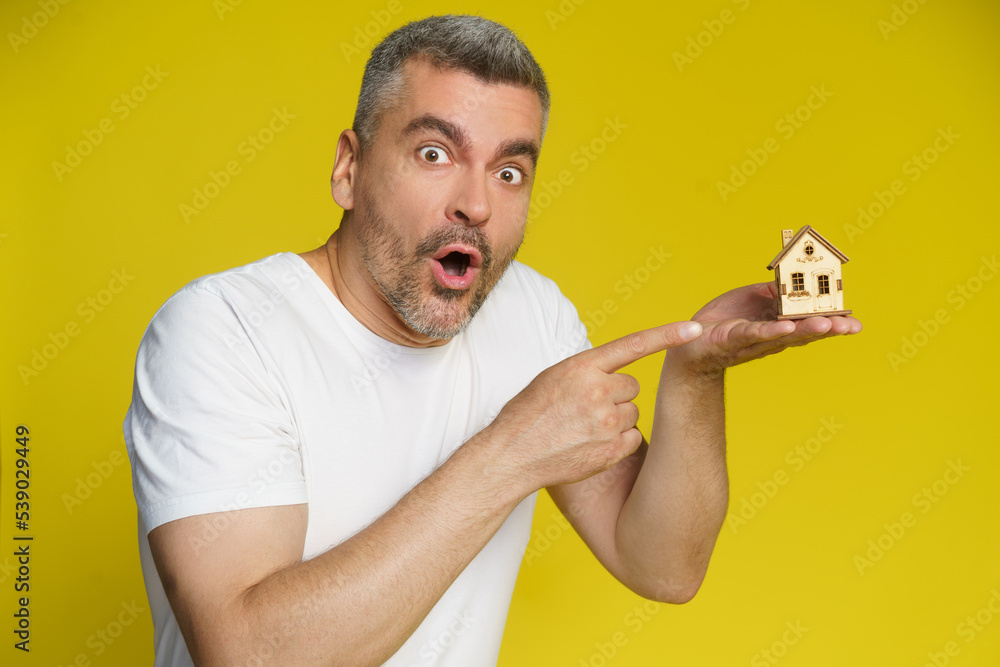 Pointing at little house layout handsome middle aged man shocked or ...