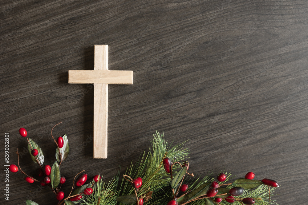 Simple wood cross with border of evergreen boughs and red berries on a ...