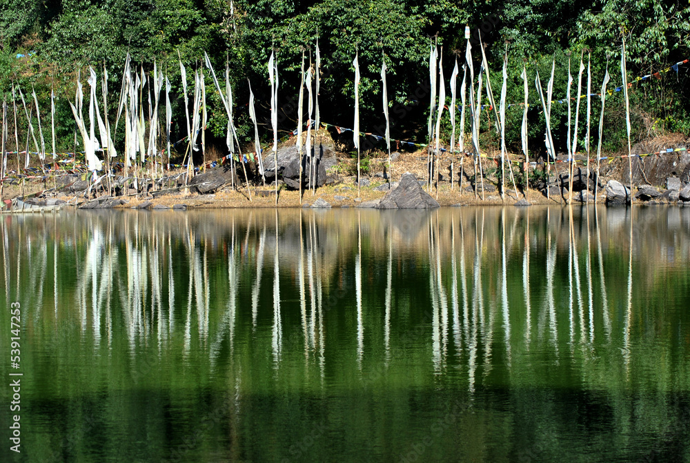 Colorful prayer flags reflects at Kartok Lake in Yuksom, Sikkim. It is ...