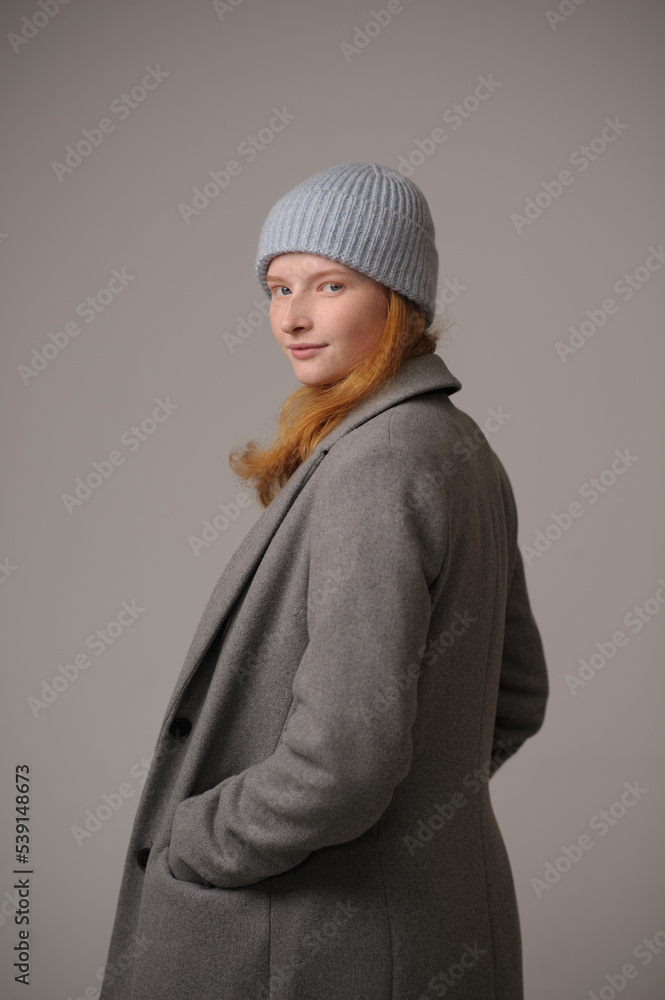 young girl model in light blue cap and gray coat isolated on grey ...