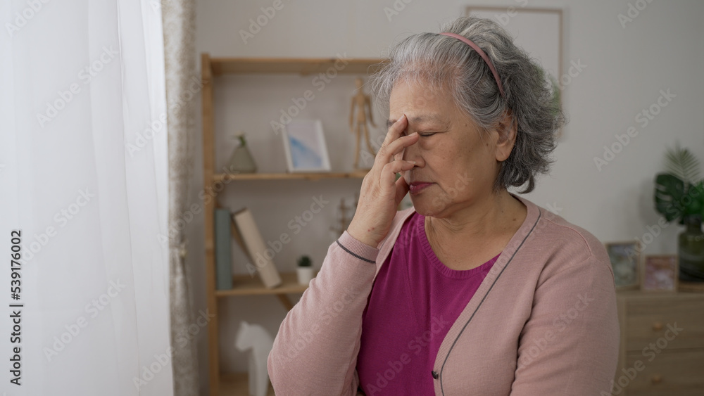 sad chinese old female is gazing out of window and rubbing her brows in ...
