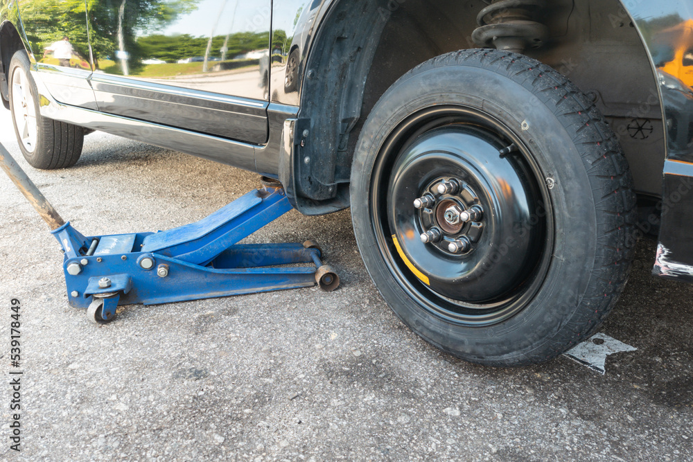 Hydraulic car jack lift car to replace punctured tyre with temporary ...