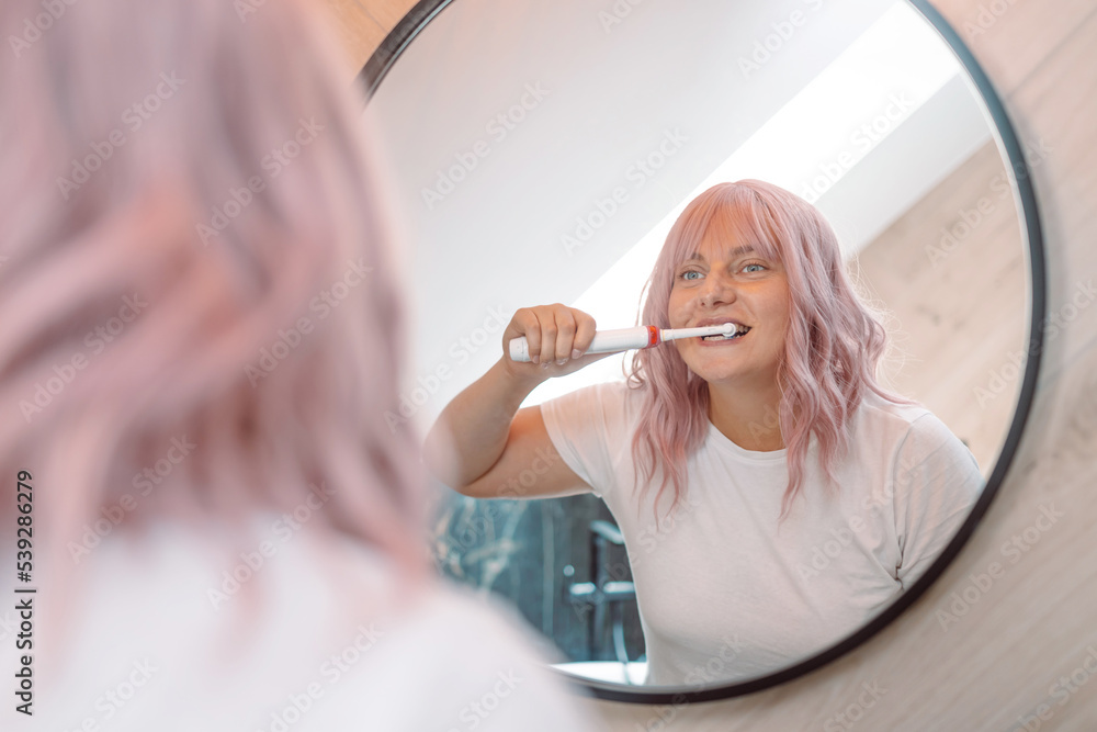 Caucasian pink hair woman brushing teeth with electric toothbrush in ...