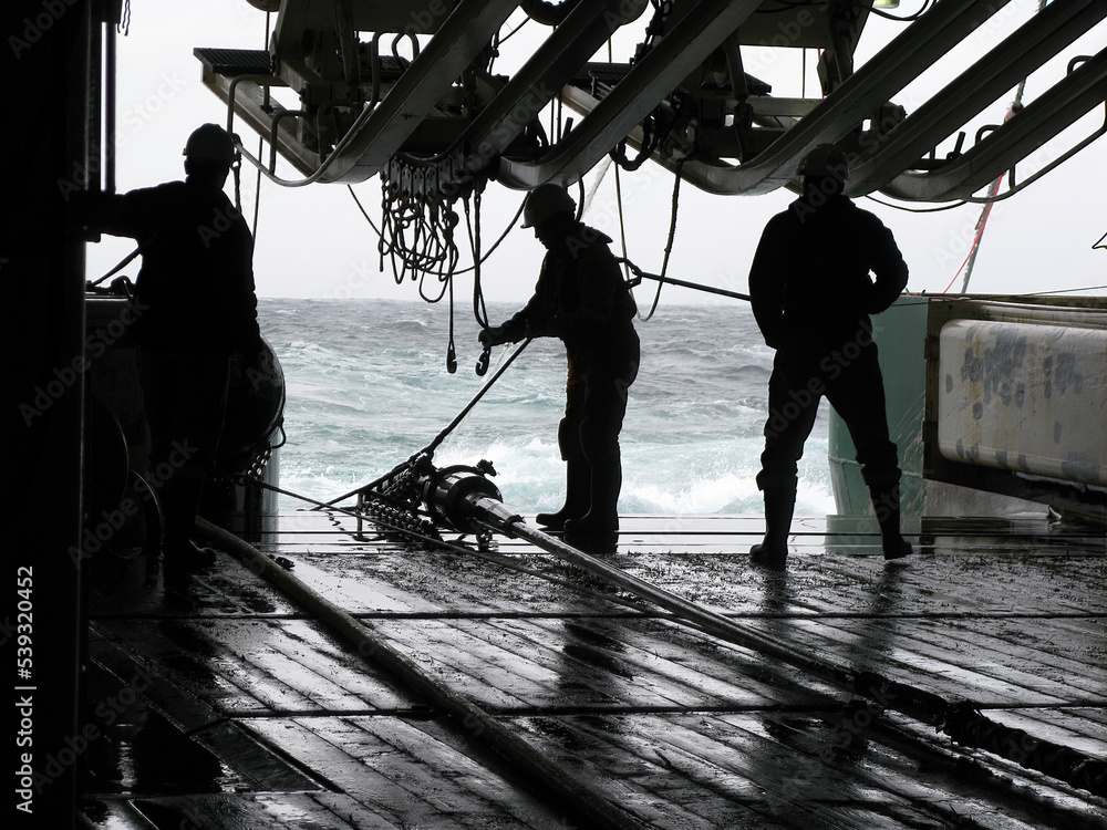 Silhouettes of persons recovering source (gun) array on seismic survey ...