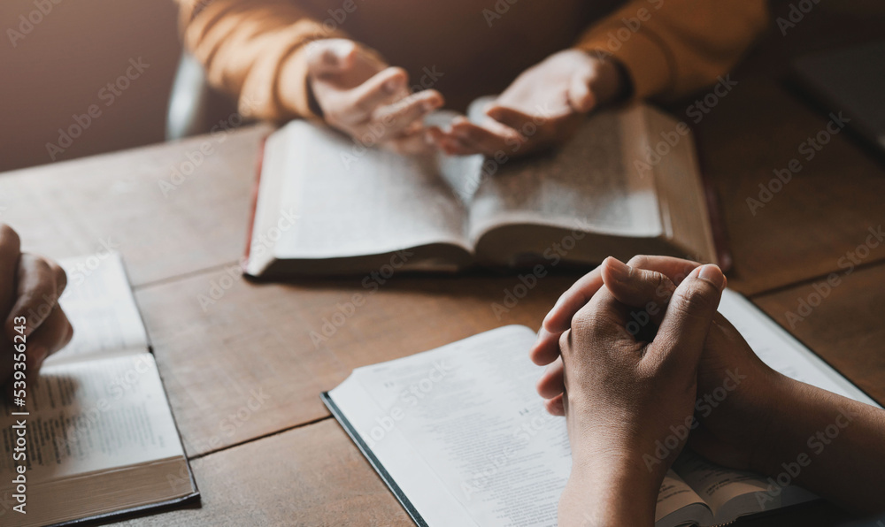 A group of Christians sit together and pray around a wooden table with ...