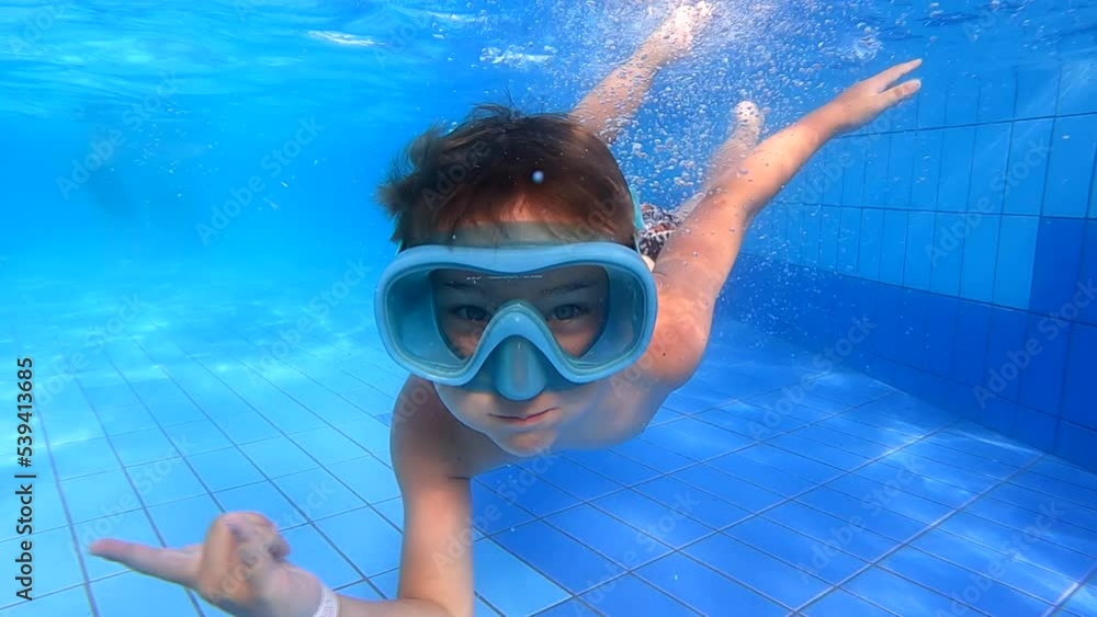 A happy child swimming underwater in the pool, showing hand gestures, a ...
