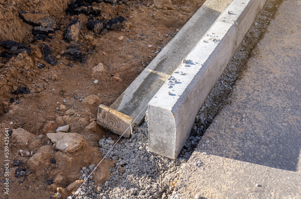 Concrete curbs installation works at road construction site. String ...