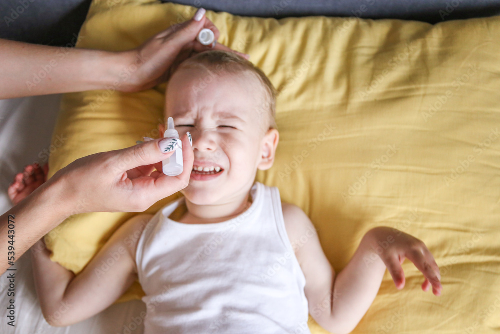 A mother treats her child's conjunctivitis with eye drops in bed. baby ...